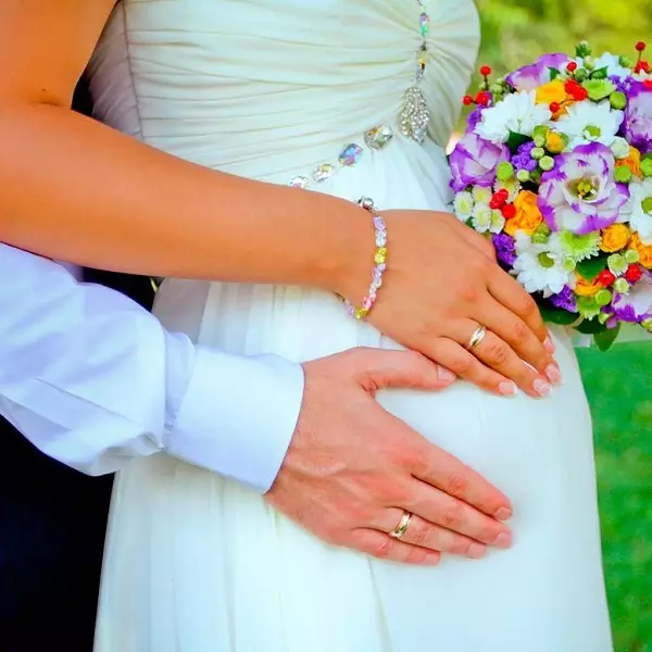 The groom hugs a pregnant bride